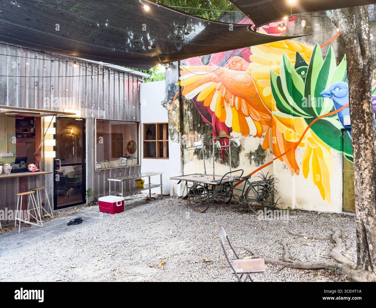 Outdoor patio with vibrant mural of colorful birds, rustic furniture, Hin bus depot George town ...