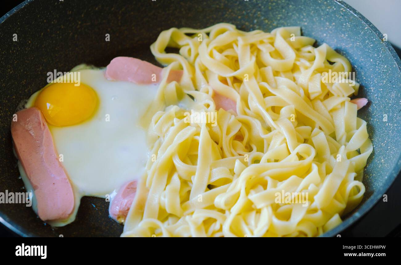 Close-up featuring pasta, fried egg, and sausages sizzling in a frying ...