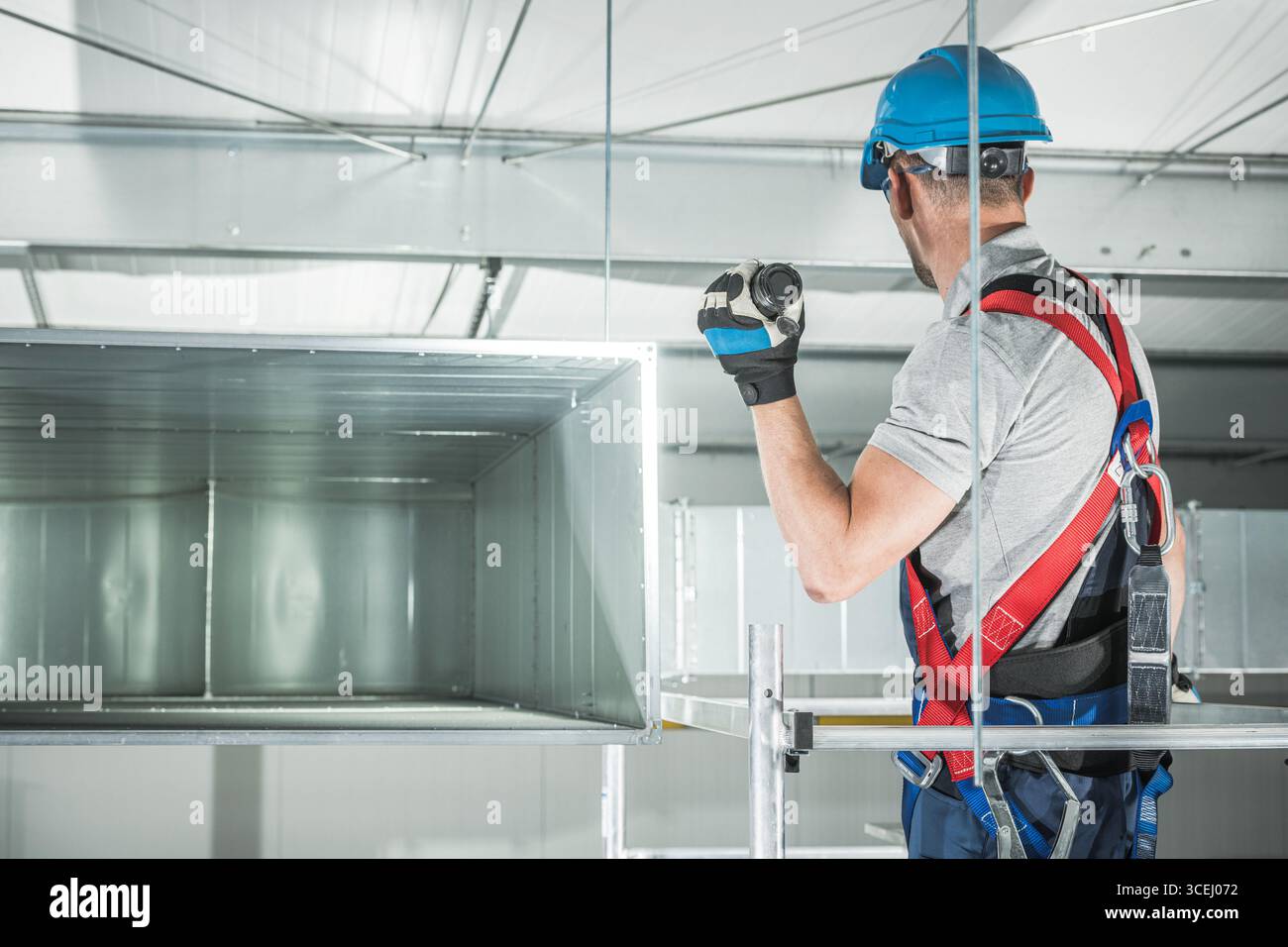 A construction HVAC worker in a safety harness and hard hat is ...