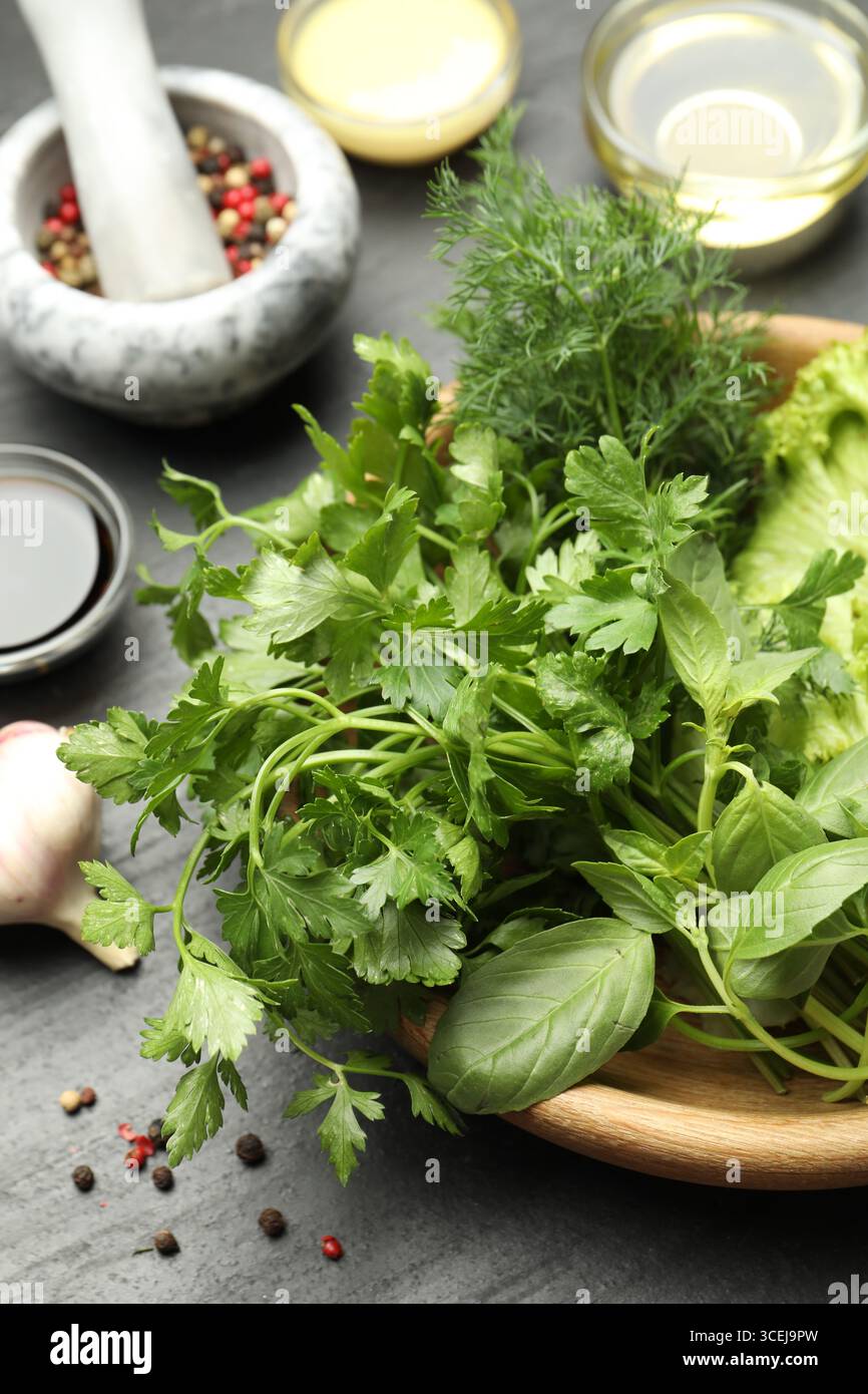 Different aromatic herbs in bowl and products on dark textured table ...