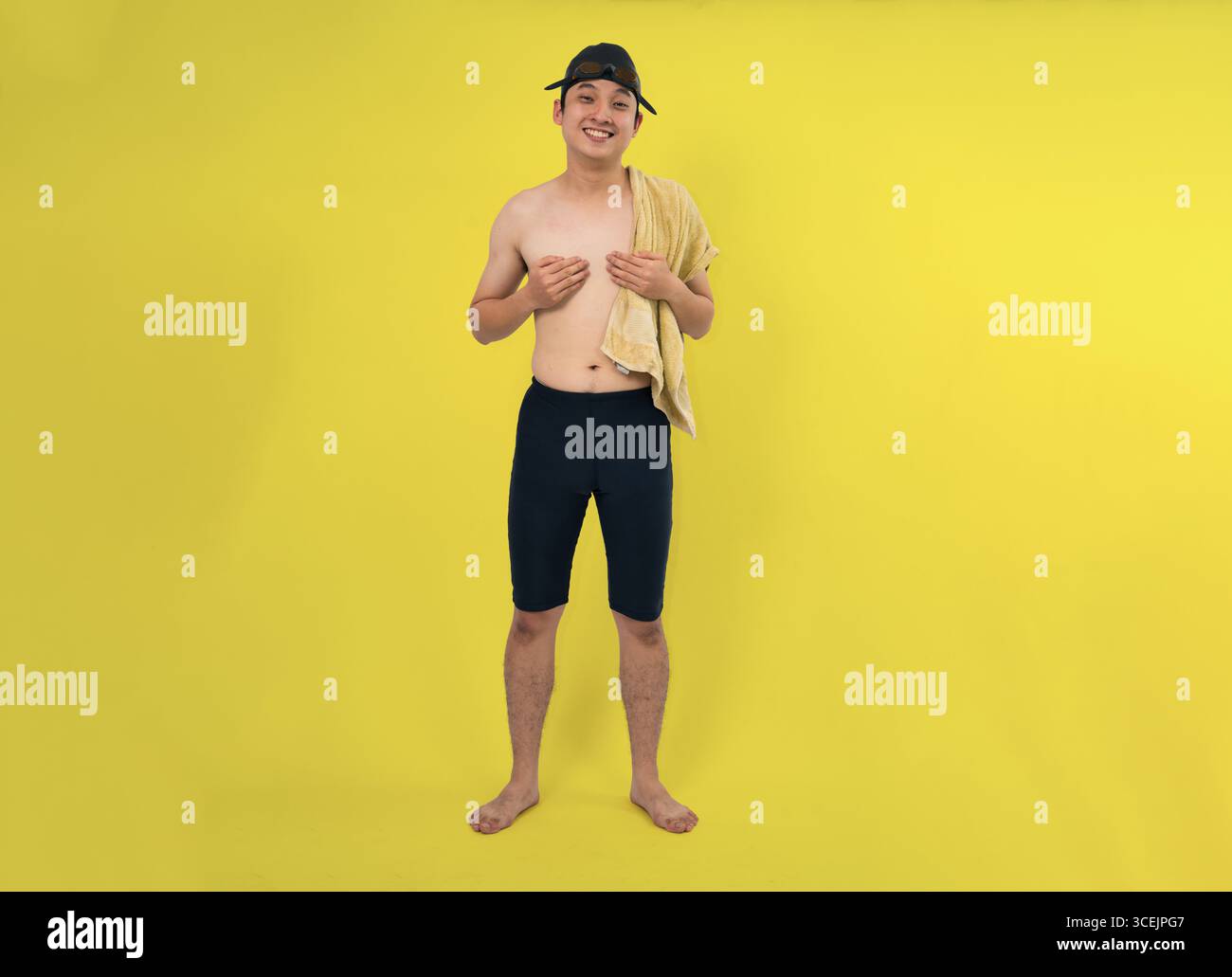confident swimmer holding towel against yellow background in studio ...