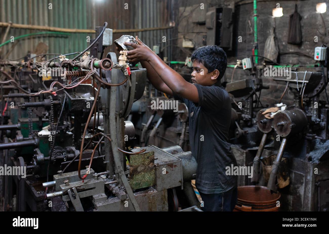 A teenage boy seen working with heavy machinery at a metal nut factory ...