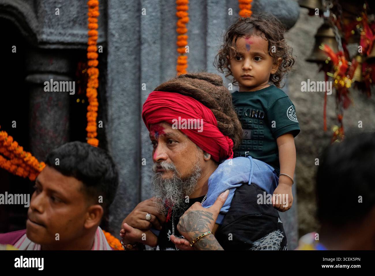 A Sadhu or Hindu holy man carries a baby on his shoulder during the ...