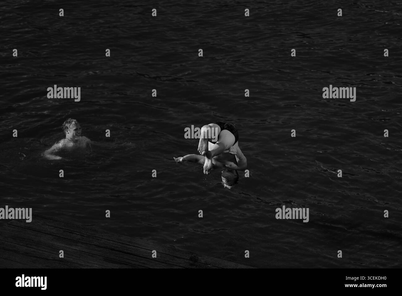 A diver tucks into a tight flip above a dark canal while a swimmer ...