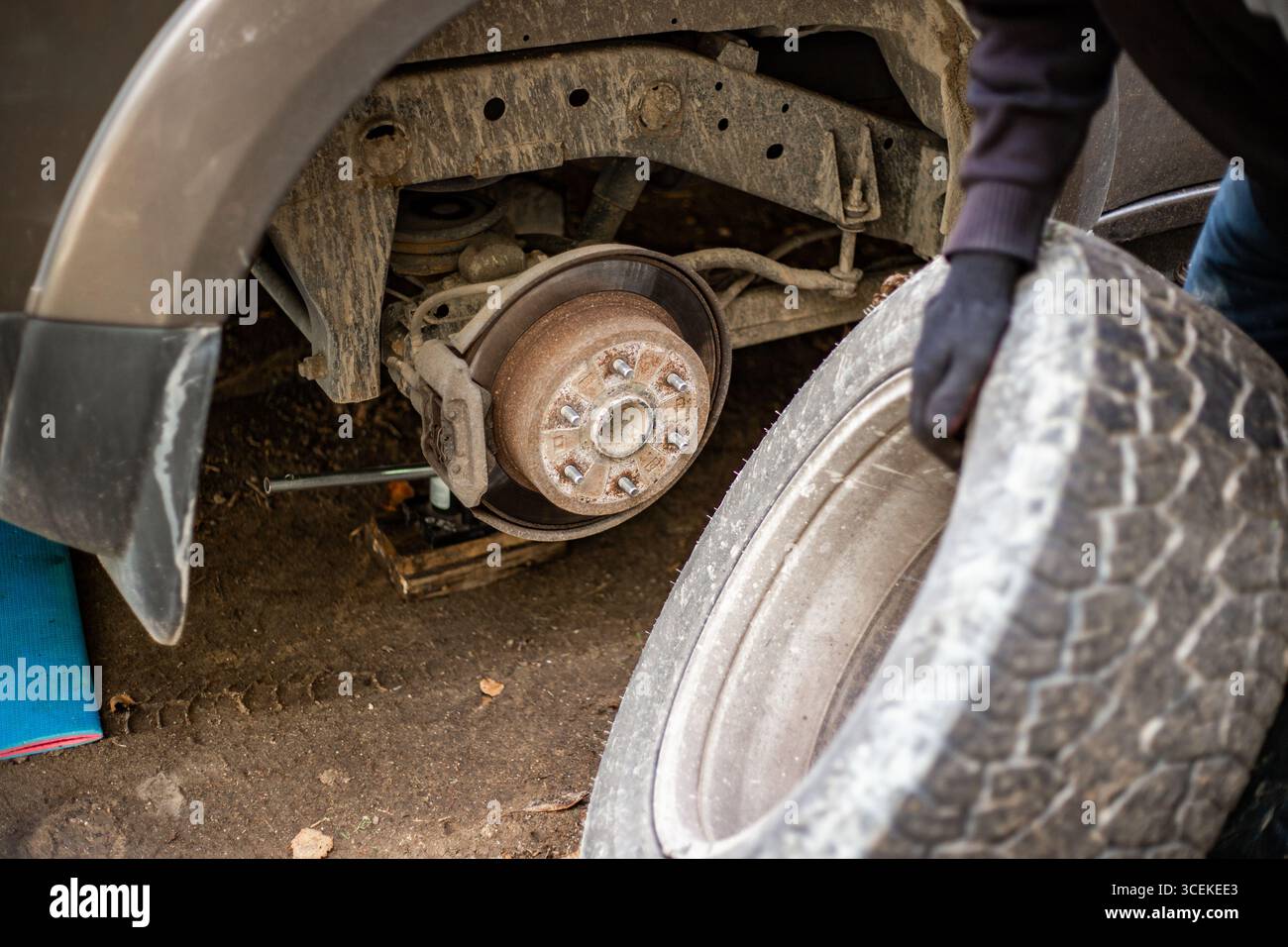 Mechanic's gloved hand holding tire next to car with wheel removed ...