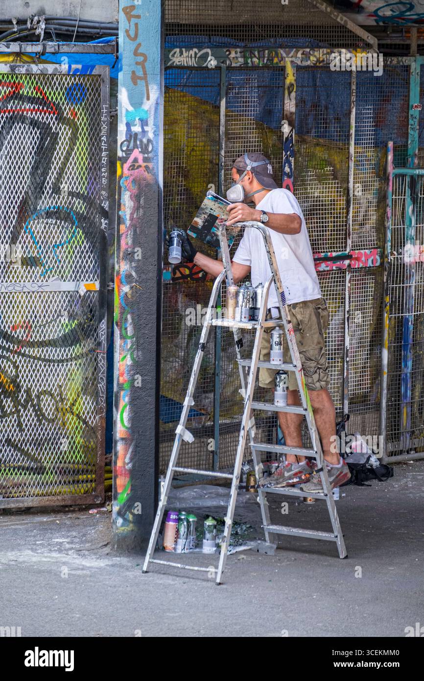 Male graffiti artist standing on ladder painting column with spray ...