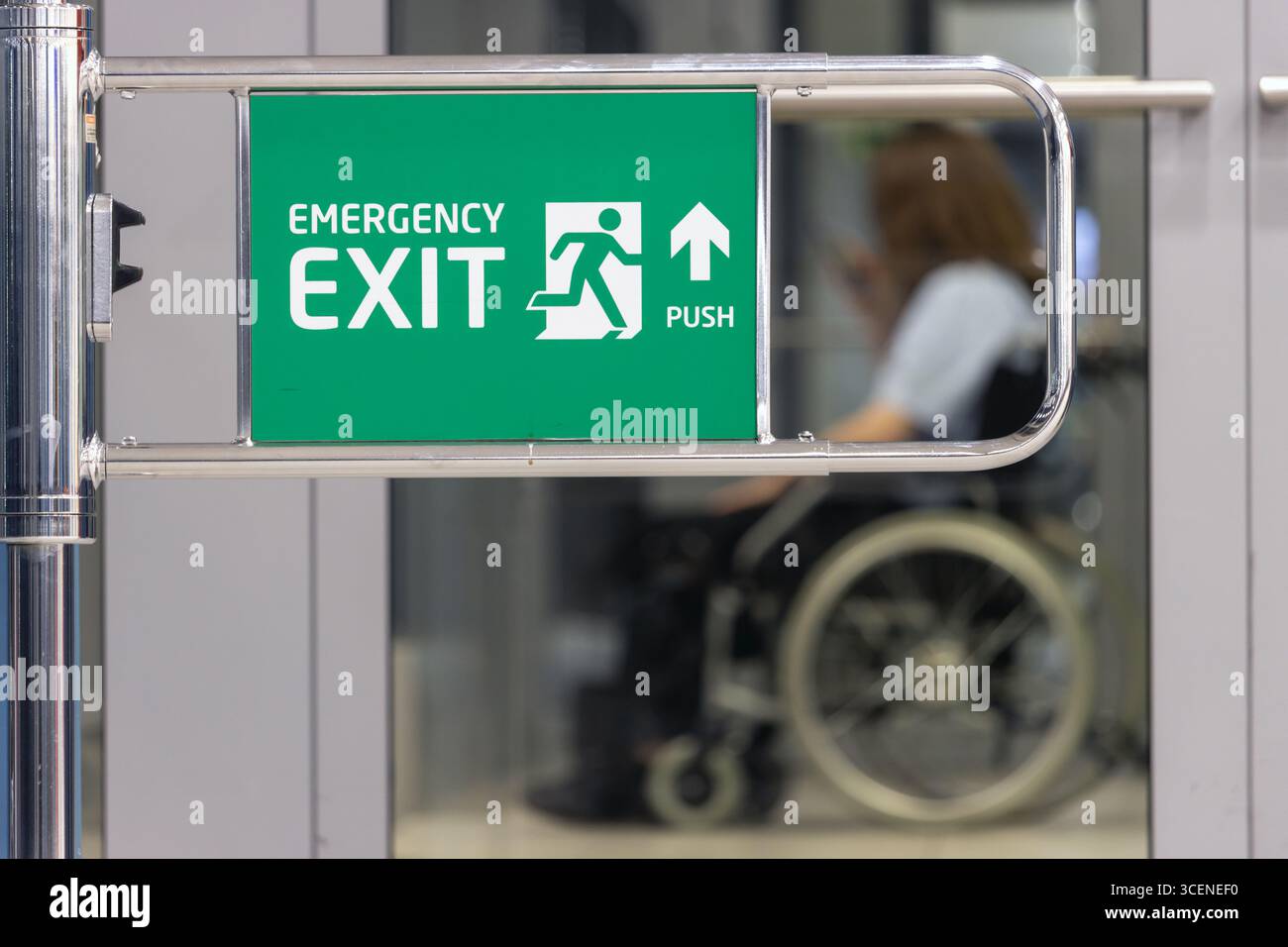 Green emergency exit sign on metal gate indoors with disabled person in ...