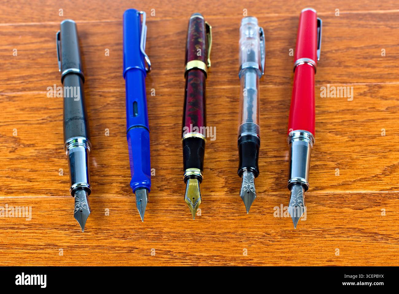 Five fountain pens, of various colors, laying on a table with their ...