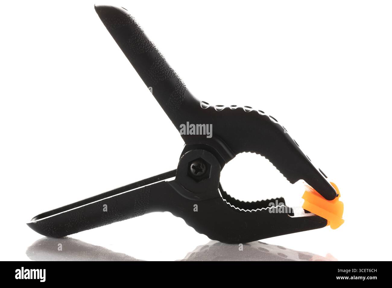 A black spring clamp with an orange tip on a white background. The ...