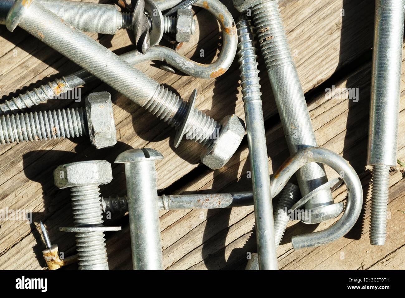 A collection of various metal bolts, screws, and nuts arranged on a wooden surface. The hardware ...