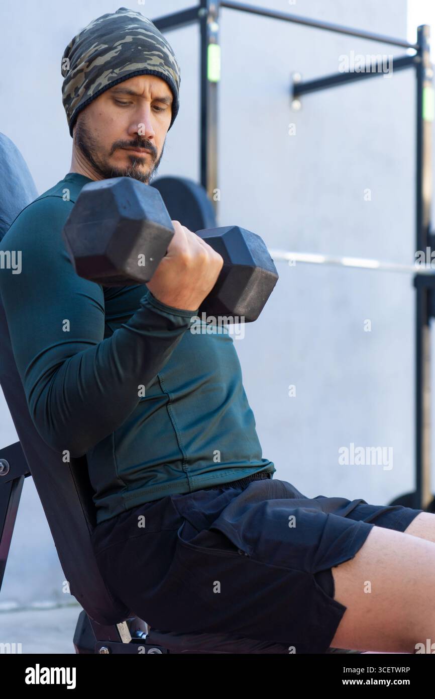 Focused athlete lifts dumbbells, performing bicep curls while seated on ...
