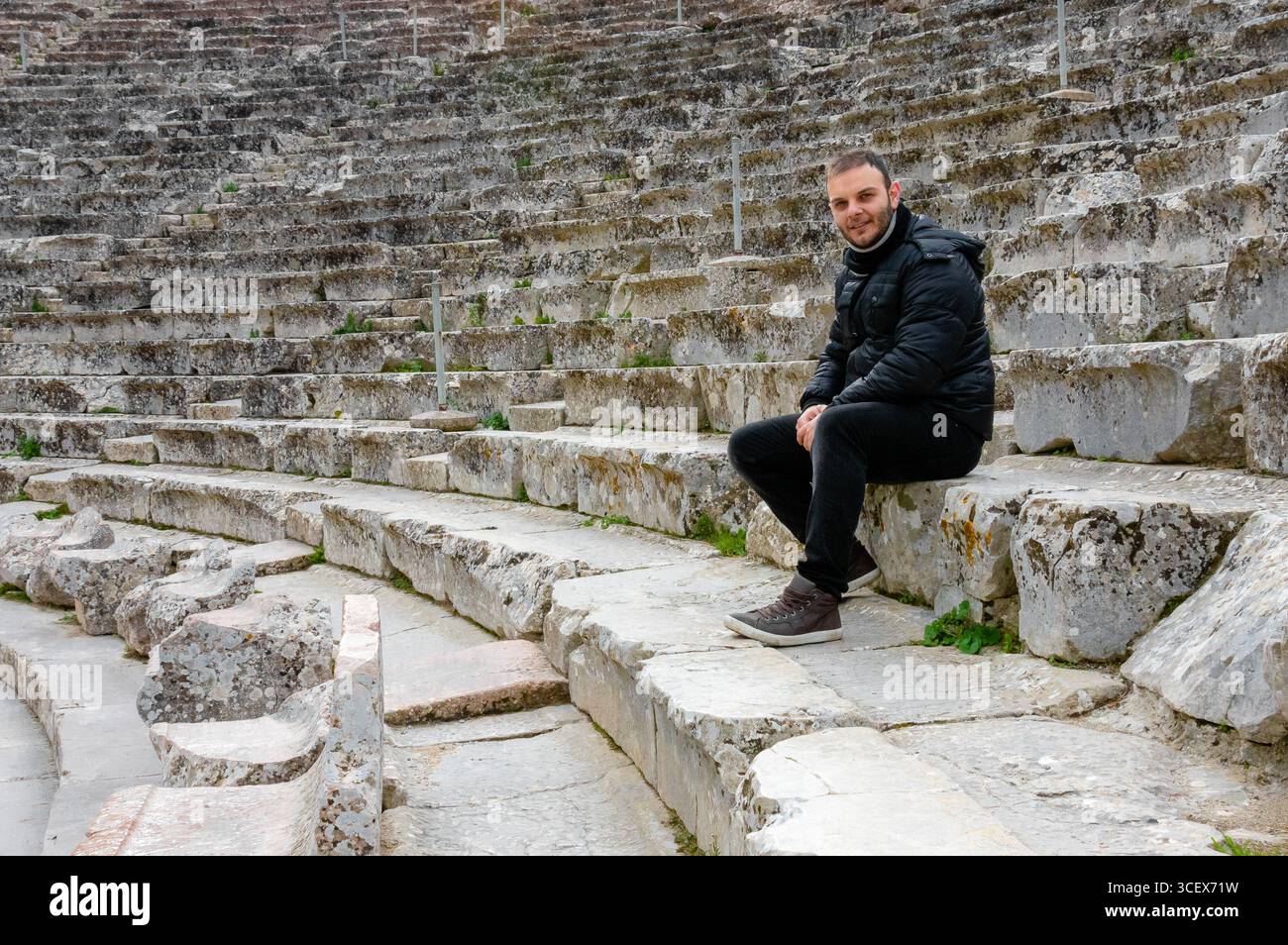 Smiling man sitting on stone seats at the Ancient Epidaurus Theater in ...