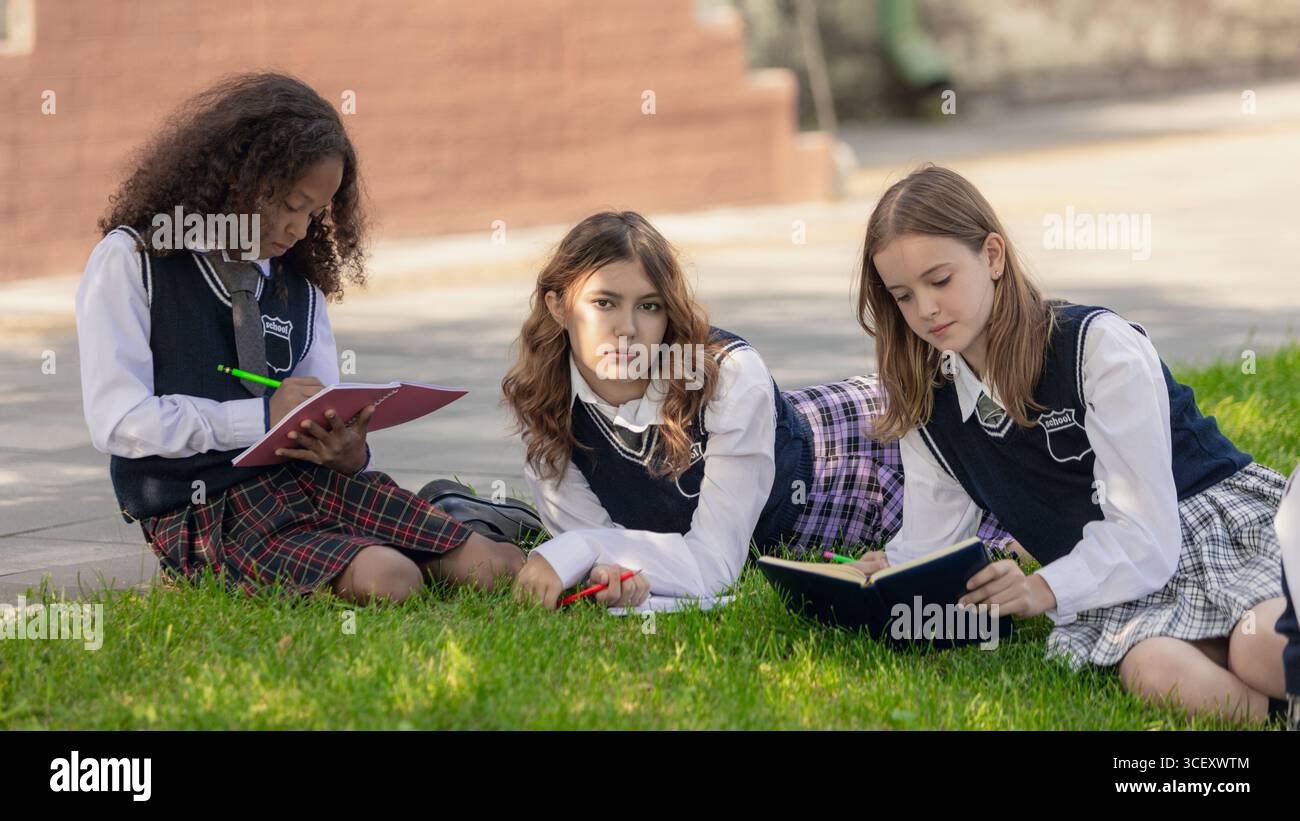 Teen girls in school uniforms reading and writing with serious ...