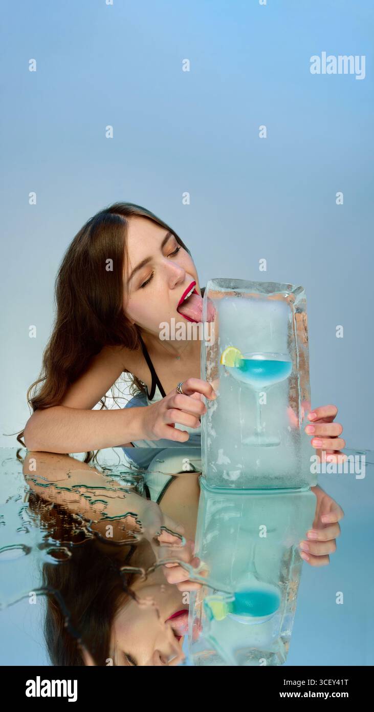 Young woman licking frozen ice block with blue cocktail inside on ...