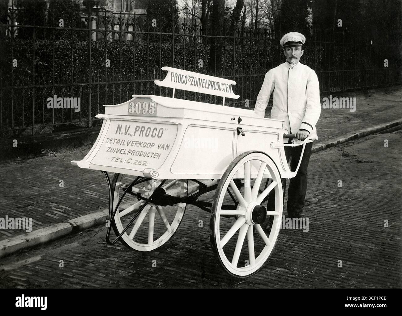 A milk vendor in a uniform jacket and cap stands by his white milk cart ...