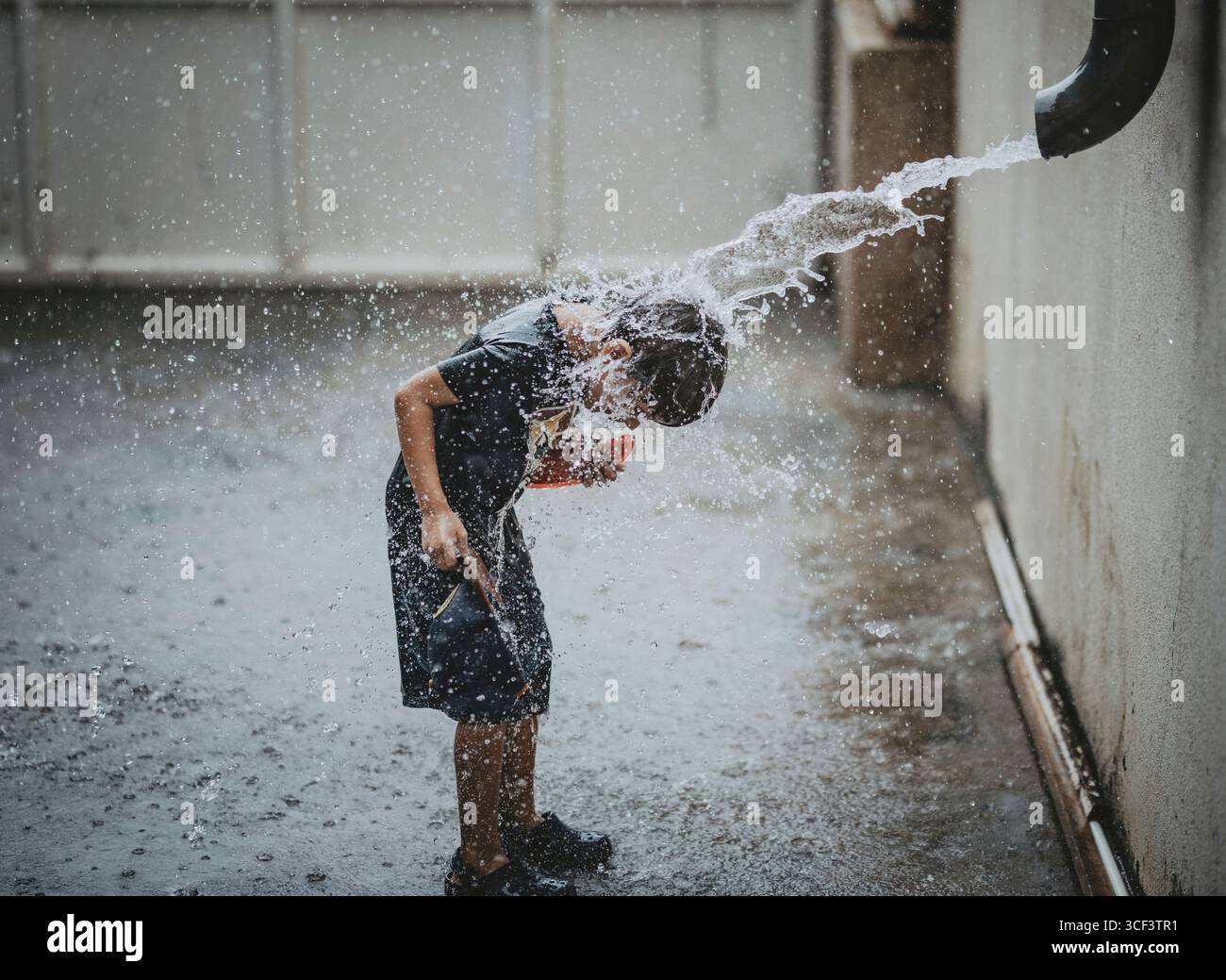 Boy stands under the gutter in the rain in the town of Tarrafal Stock ...