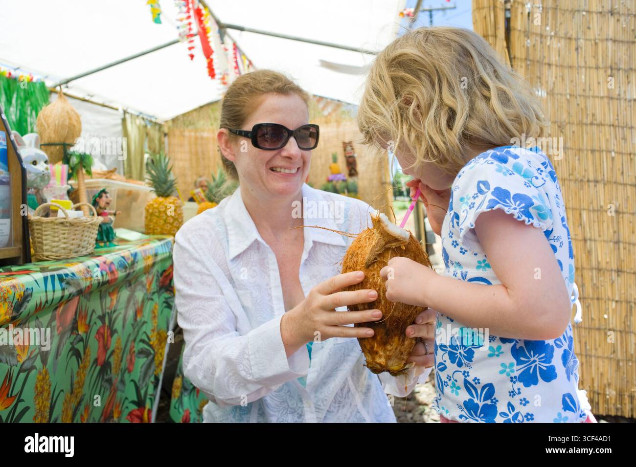 Mother holding coconut for daughter who is sipping the coconut milk ...