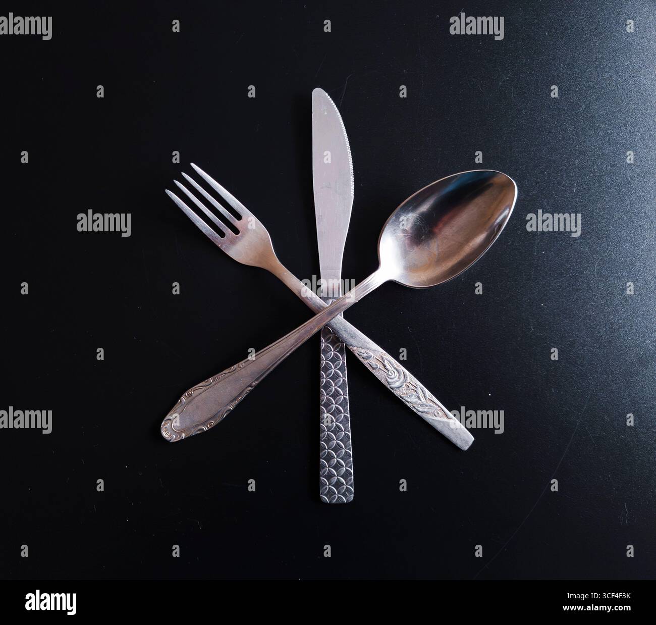 Silver fork, knife and spoon crossing each other on a black background ...