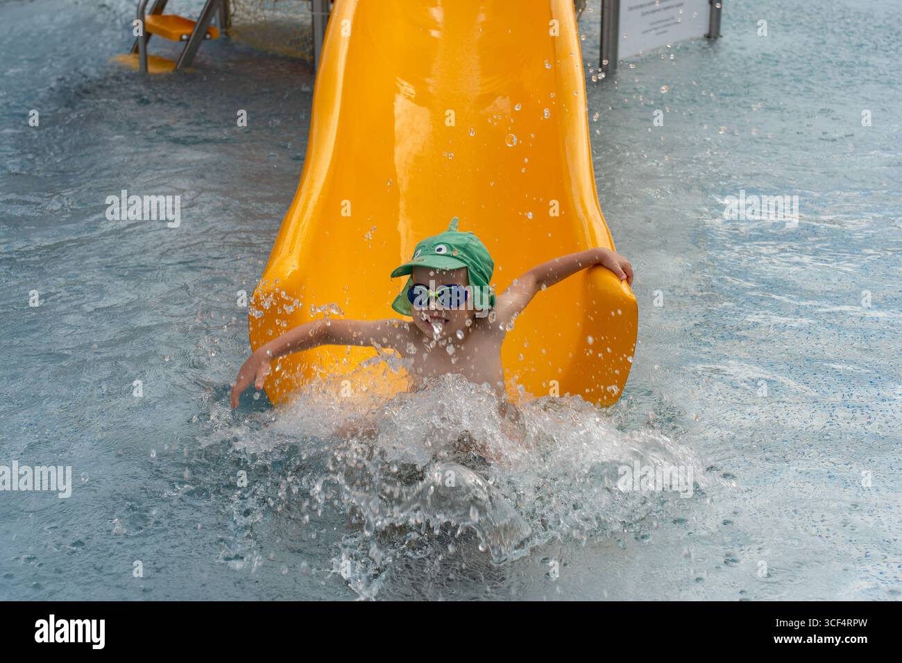 Excited young swimmer in crocodile-themed cap and blue goggles sliding ...
