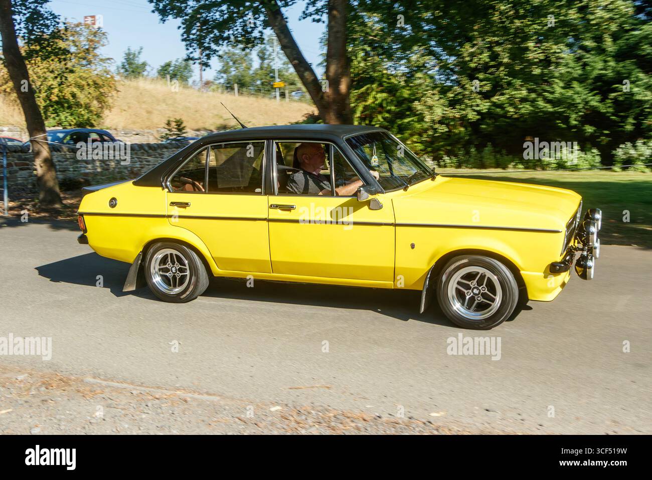 Side view of a classic yellow retro mk 2 Ford Escort car driving on a ...
