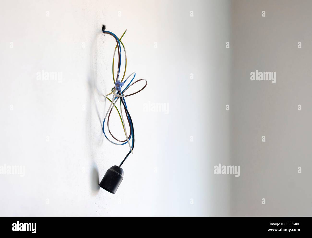 Electrical wires hanging from a white wall, featuring a bulb holder ...