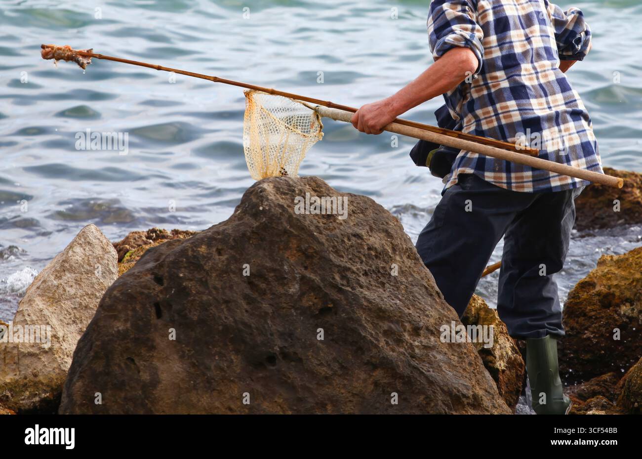 Fisherman wearing rubber boots and gripping a simple wooden fishing rod ...