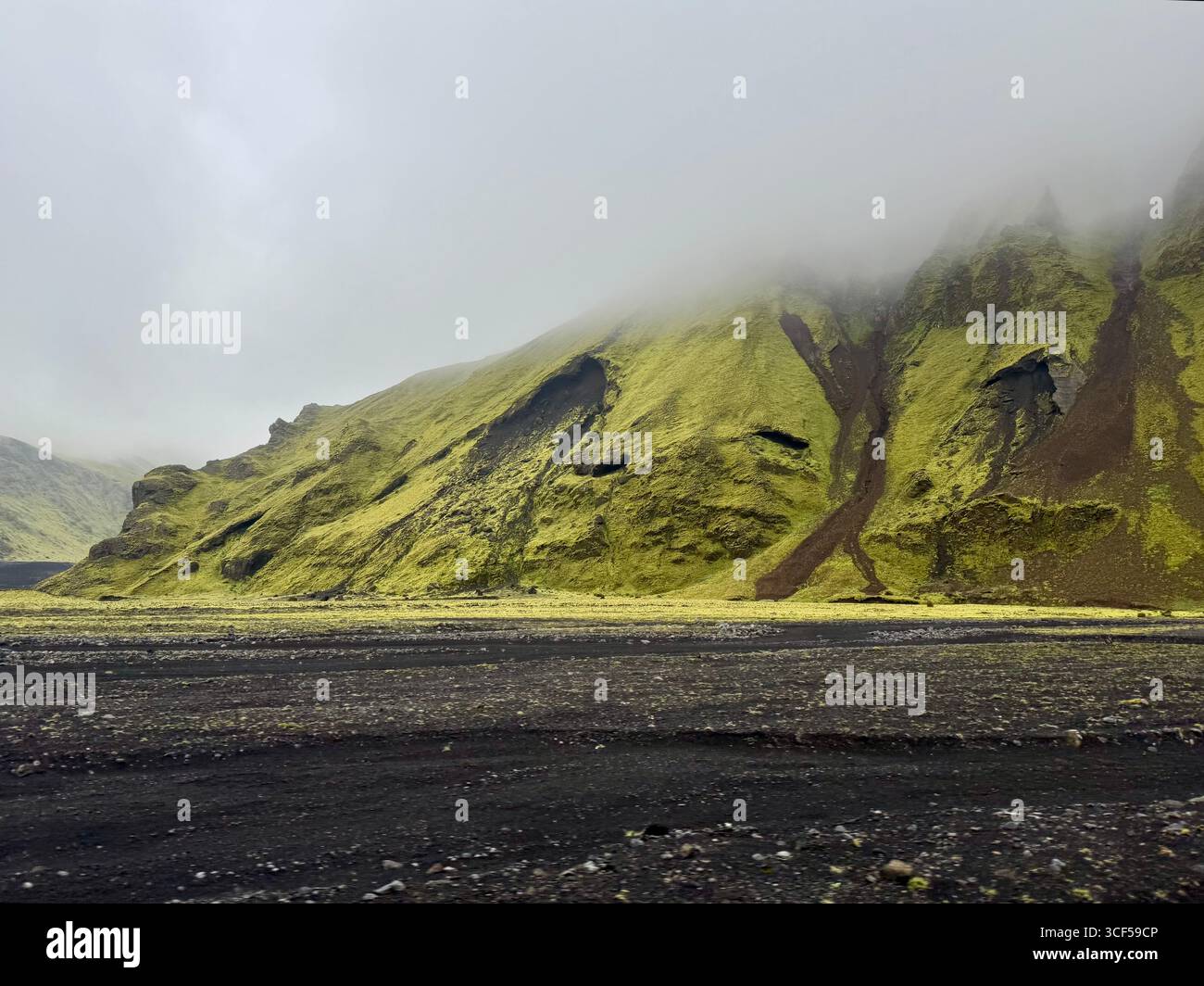 Low clouds covering the tops of moss covered volcanic hills amid black ...