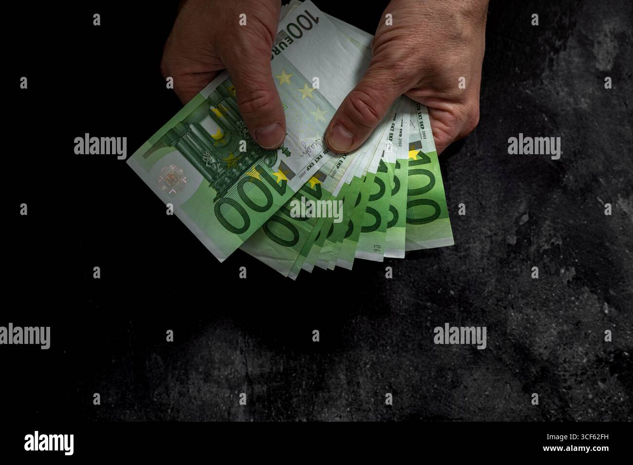 100 euro banknotes in hand on black background, man paying cash, rolled ...