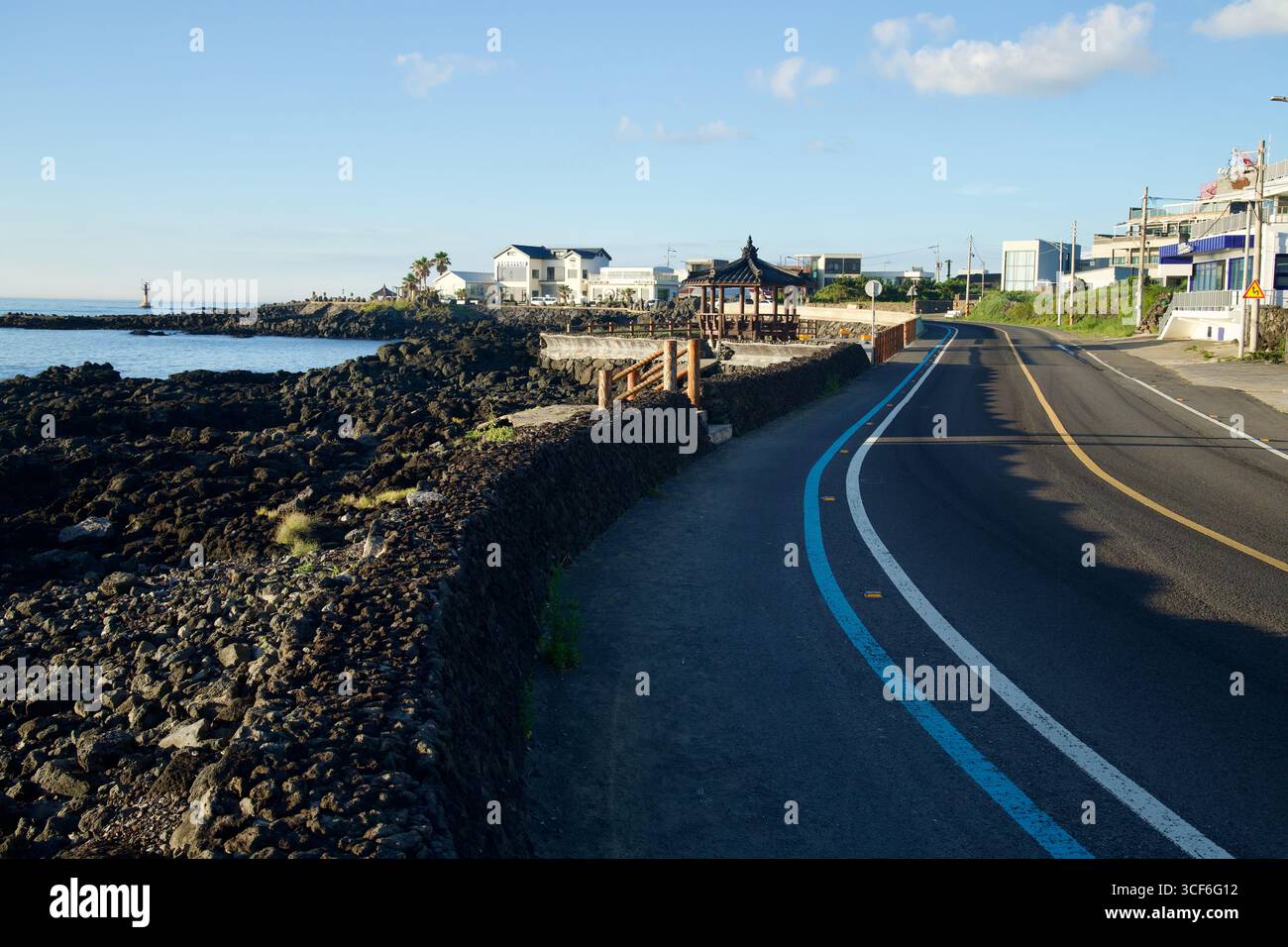 A blue‑striped bike lane and two‑lane road follow a basalt seawall past ...
