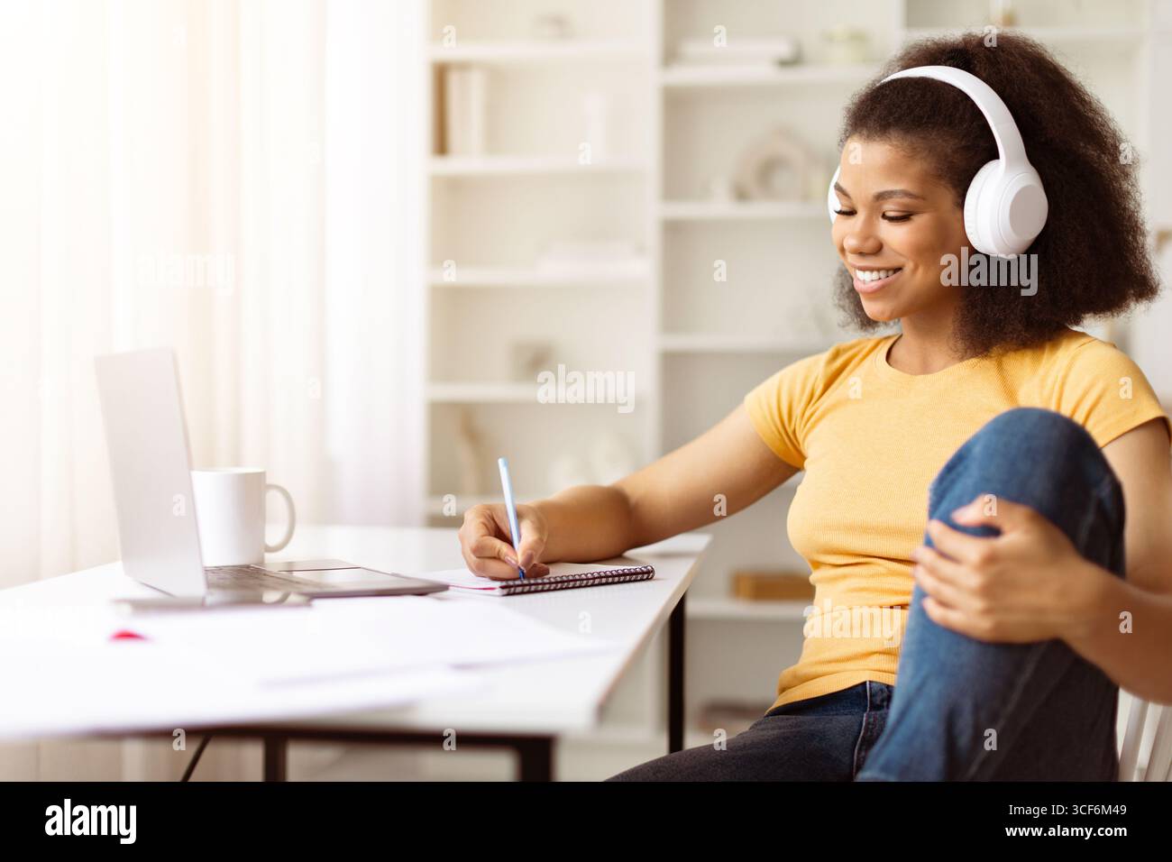 Smiling African American woman with headphones writing notes while ...