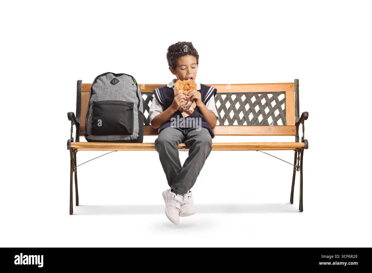 Schoolboy sitting on a bench and eating a pastry for breakfast isolated ...