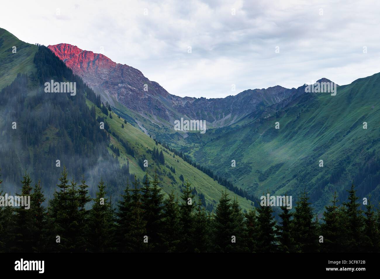 19 July 2025, Austria, Berwang: Landscape photograph of the red glowing rugged rock face in ...