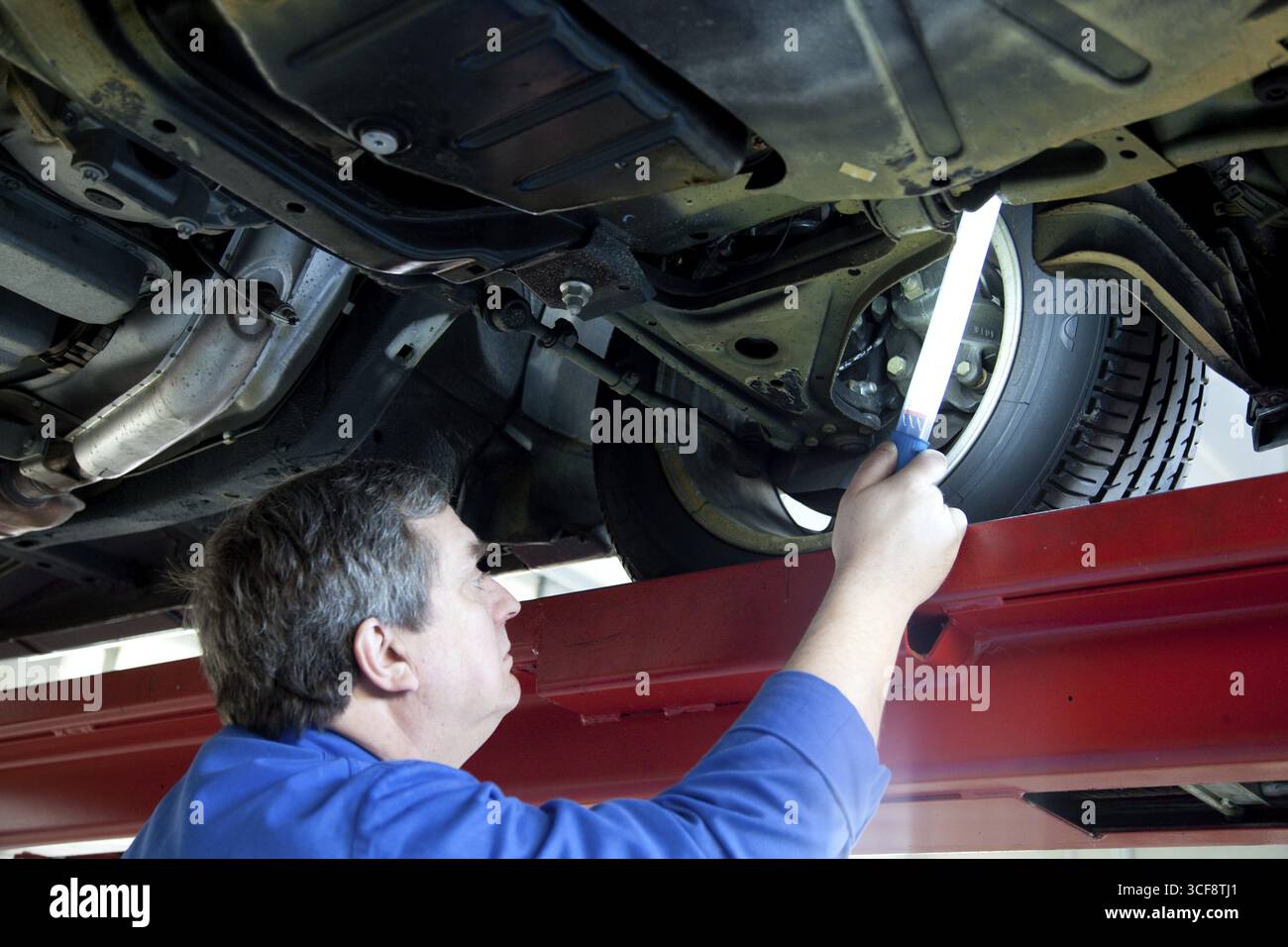 Master Craftsman of motor vehicle mechanics inspecting a car from below ...