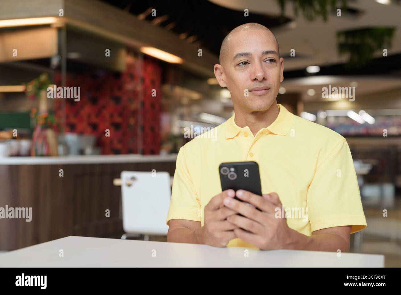 Portrait of a mature bald Italian man sitting indoors at a modern food ...