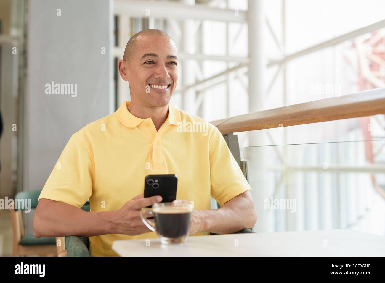 Confident mature Italian bald man sitting at a stylish cafe using phone ...