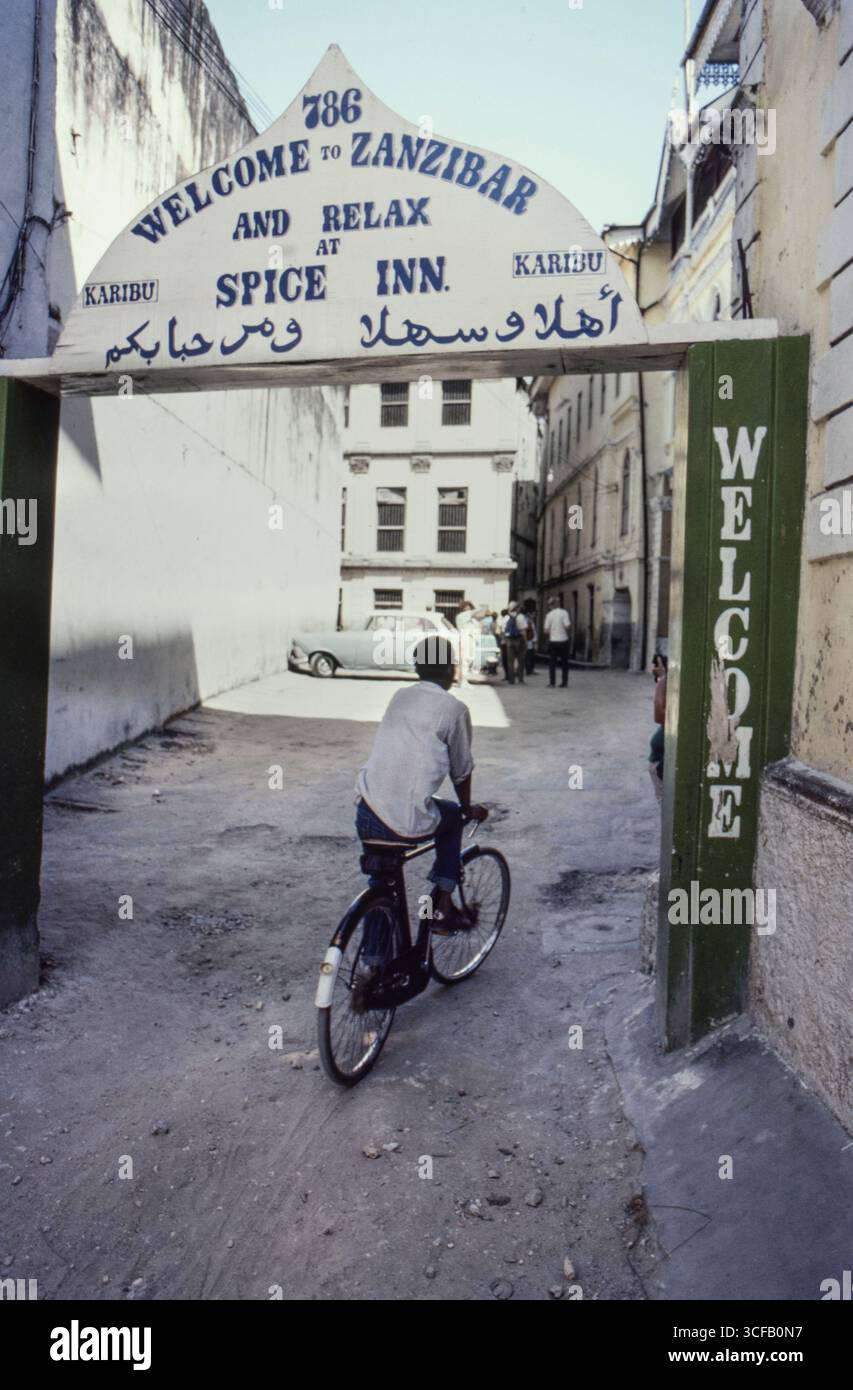 Man riding a bicycle under a sign welcoming vistors to Zanzibar and to ...