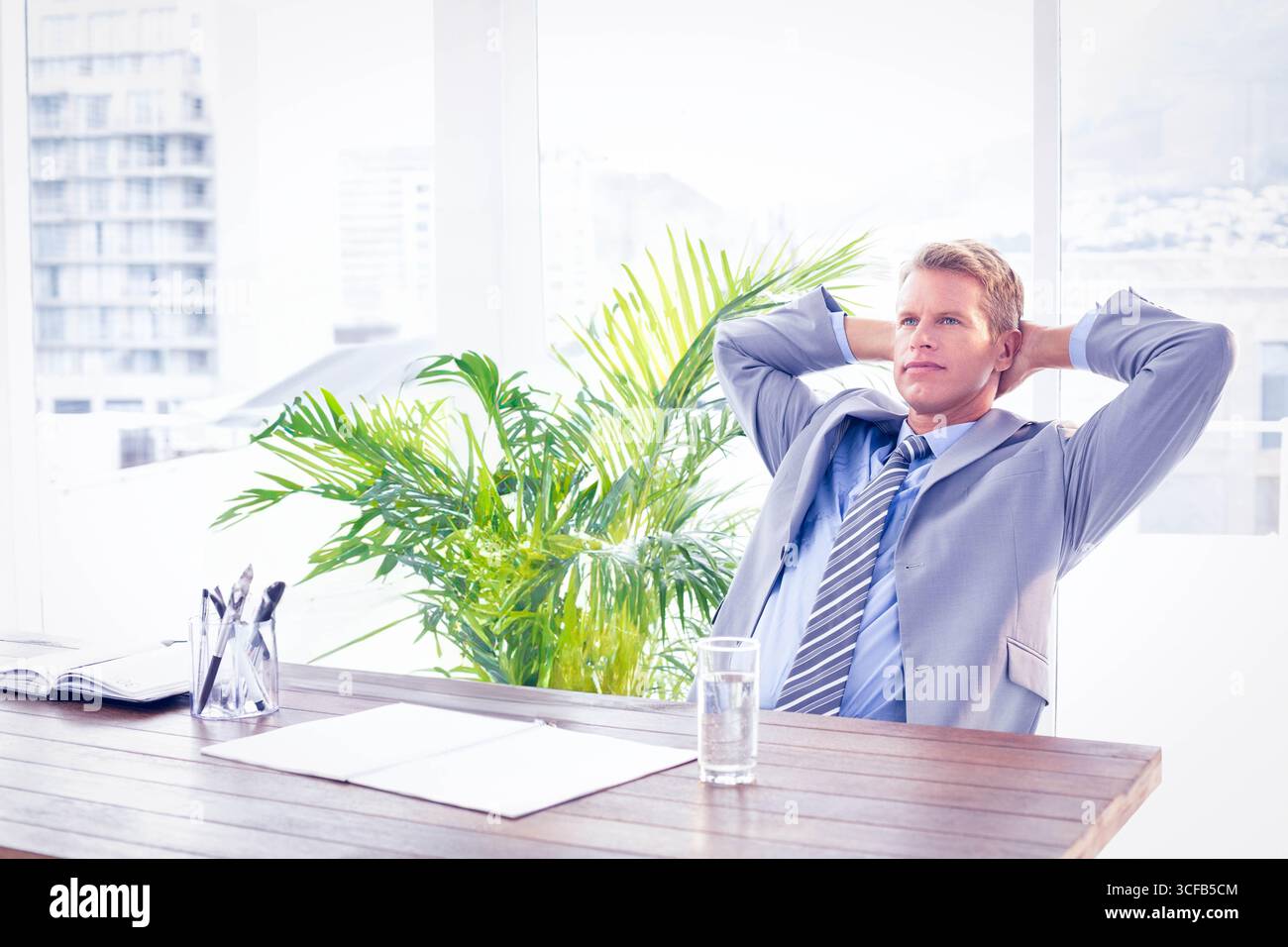 Mature man leaning back in chair at wooden desk with documents and ...