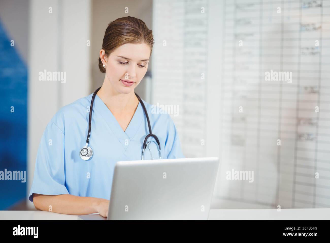 female nurse typing on silver laptop behind reception counter ...