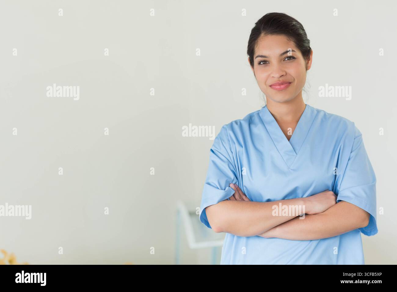 Female nurse standing with folded arms at clinic wall wearing light ...