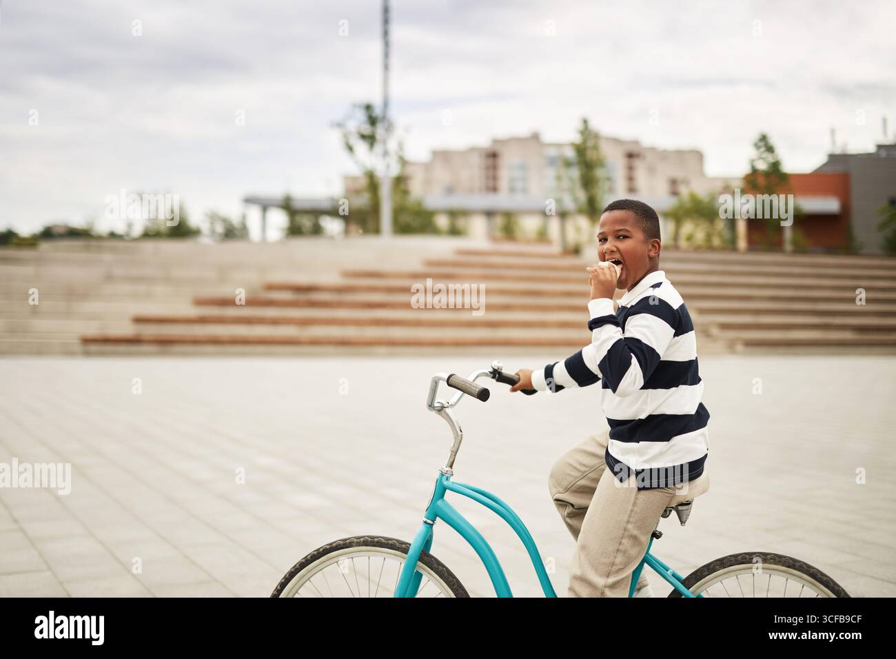 Black boy riding bicycle outdoors, turning head and looking back while ...