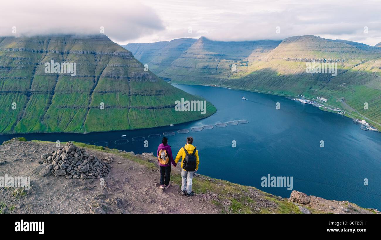 Hikers stand atop a rugged cliff of Klakkur in the Faroe Islands ...