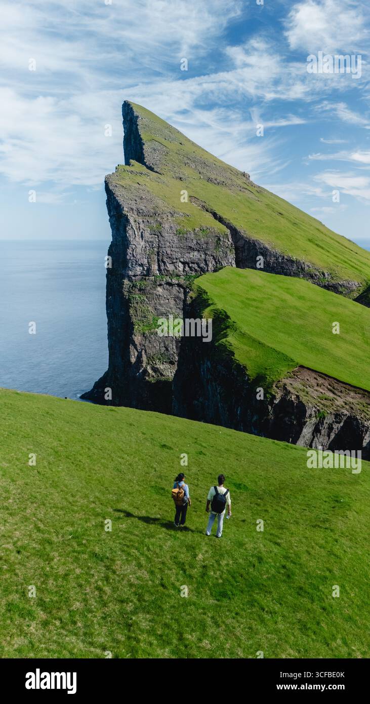 Two hikers explore the lush green landscape of the Faroe Islands ...