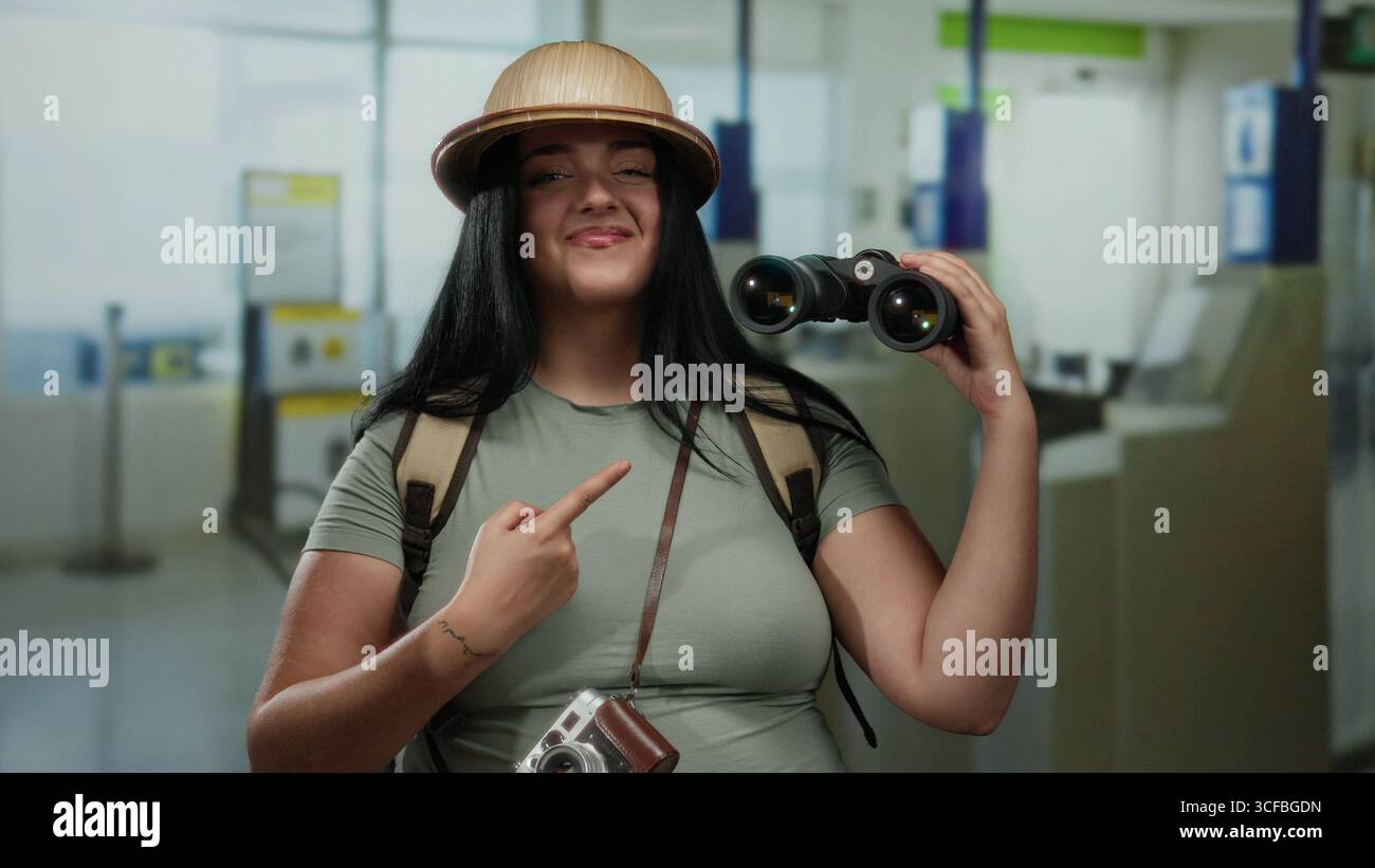 Woman in airport terminal holding binoculars wearing safari hat and ...