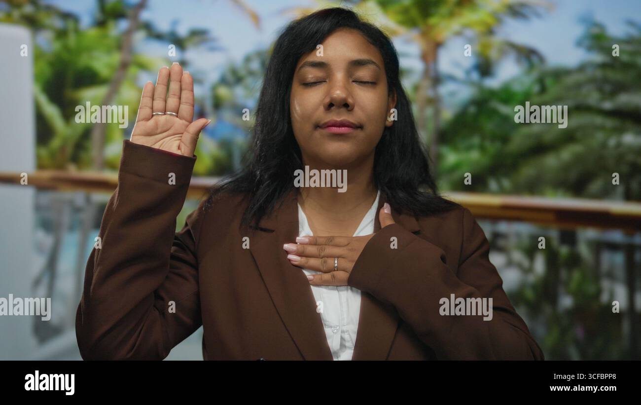 African american woman in brown blazer raises hand and places hand on ...