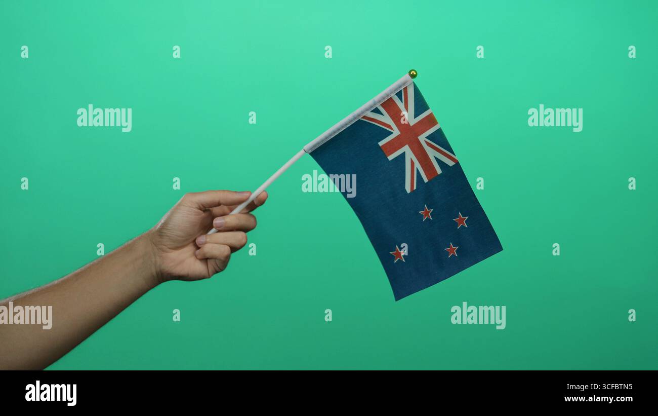 Hand holding new zealand flag against green background, representing ...
