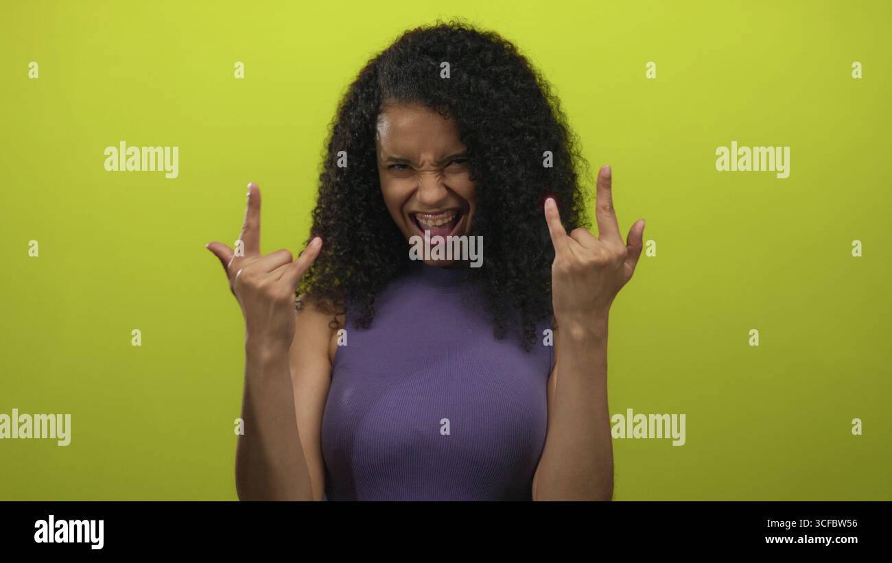 Young woman with curly hair and raised arms shows rock horns gesture in ...