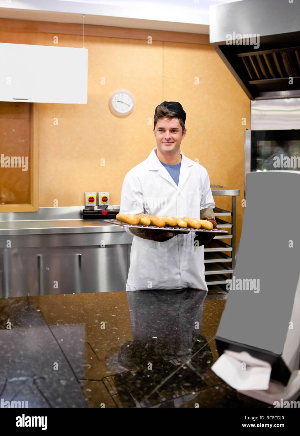 Male bakery worker wearing coat cap gloves holding bagel tray in bakery ...