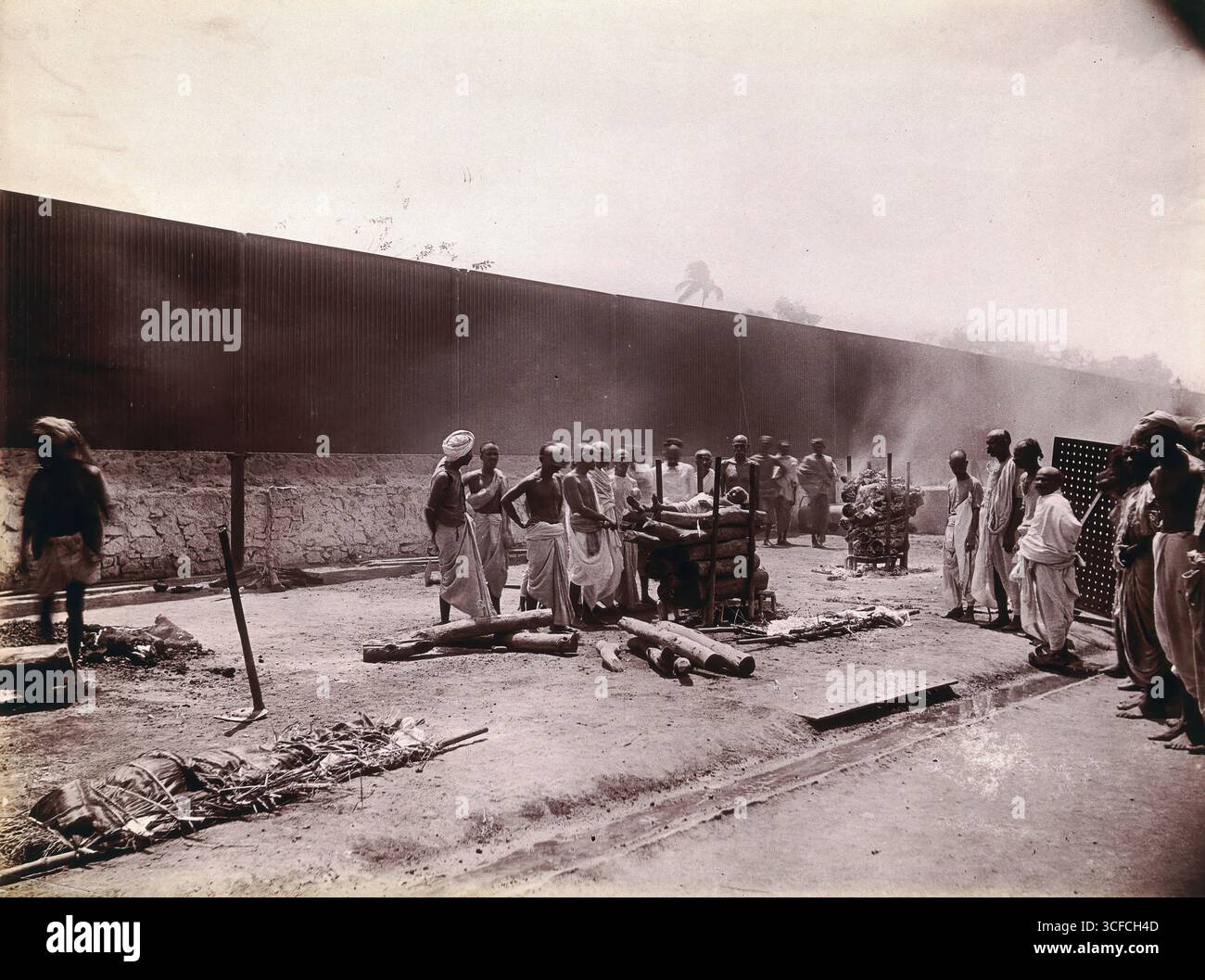 A group of men stand around the body of a man laid out on a pyre of ...