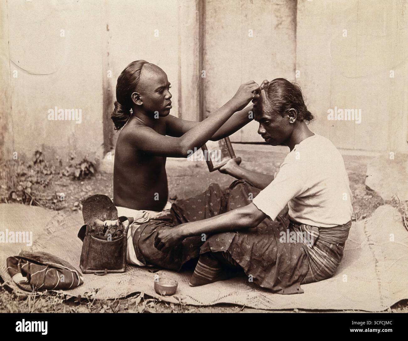 Two Indian men sitting cross-legged; one appears to be a barber and is ...