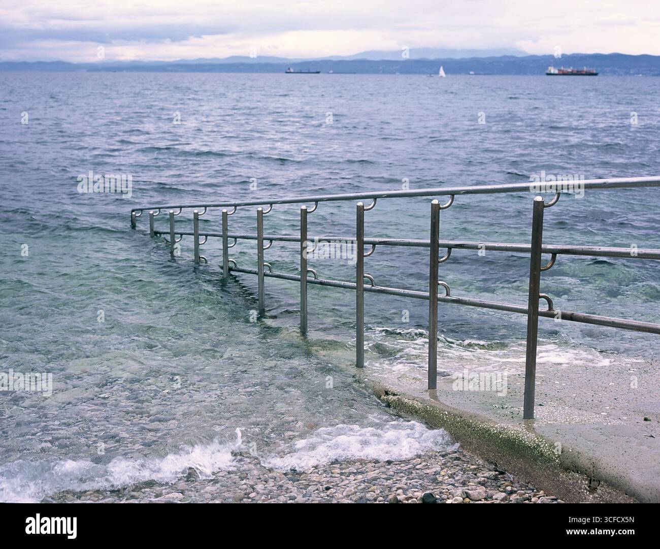 Nickel handrail entering the water, winter sea with a tanker in the ...